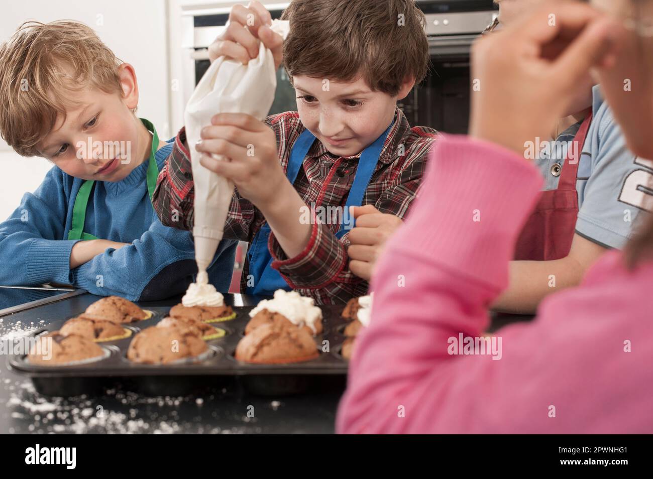 Schoolboy icing muffins with icing bag in home economics class, Bavaria ...