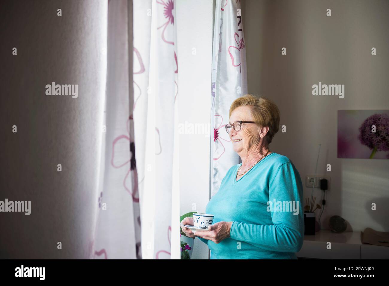 Smiling old woman looking out of window with a cup of coffee Stock ...