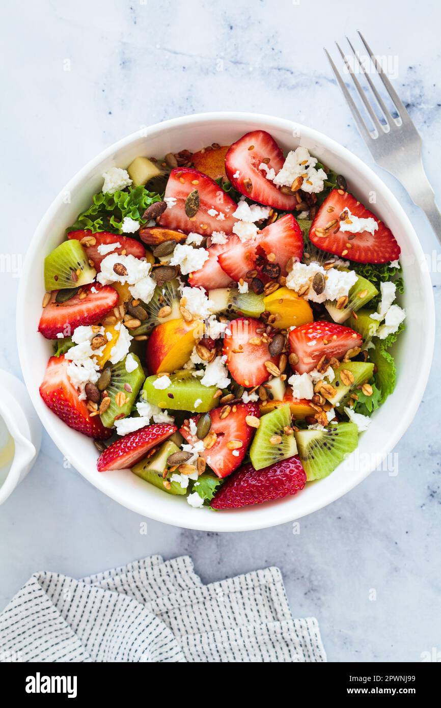 Fruit salad with feta and seeds in a white bowl on a white table ...