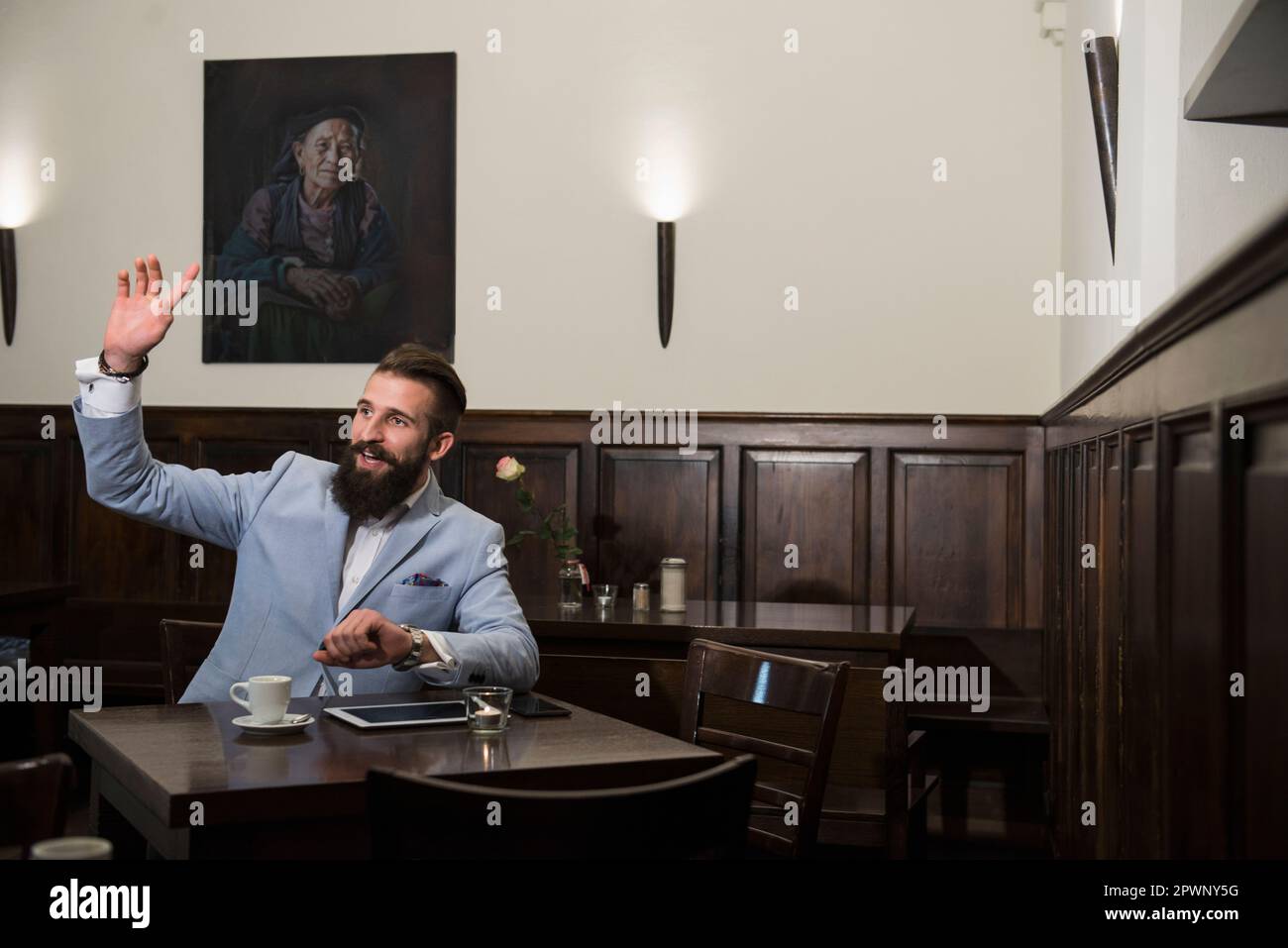 Young man in suit calling waiter at restaurant while tablet and coffee ...