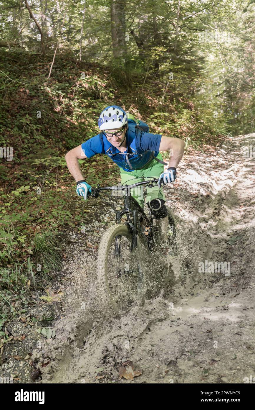 Mountain biker riding through puddle and splashing water in forest ...