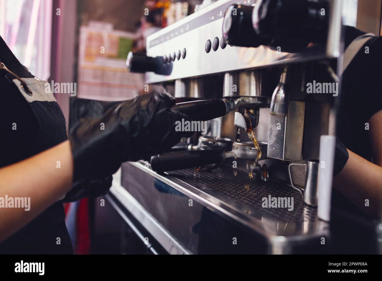 Barista in black gloves and apron rinses the holder of automatic coffee ...
