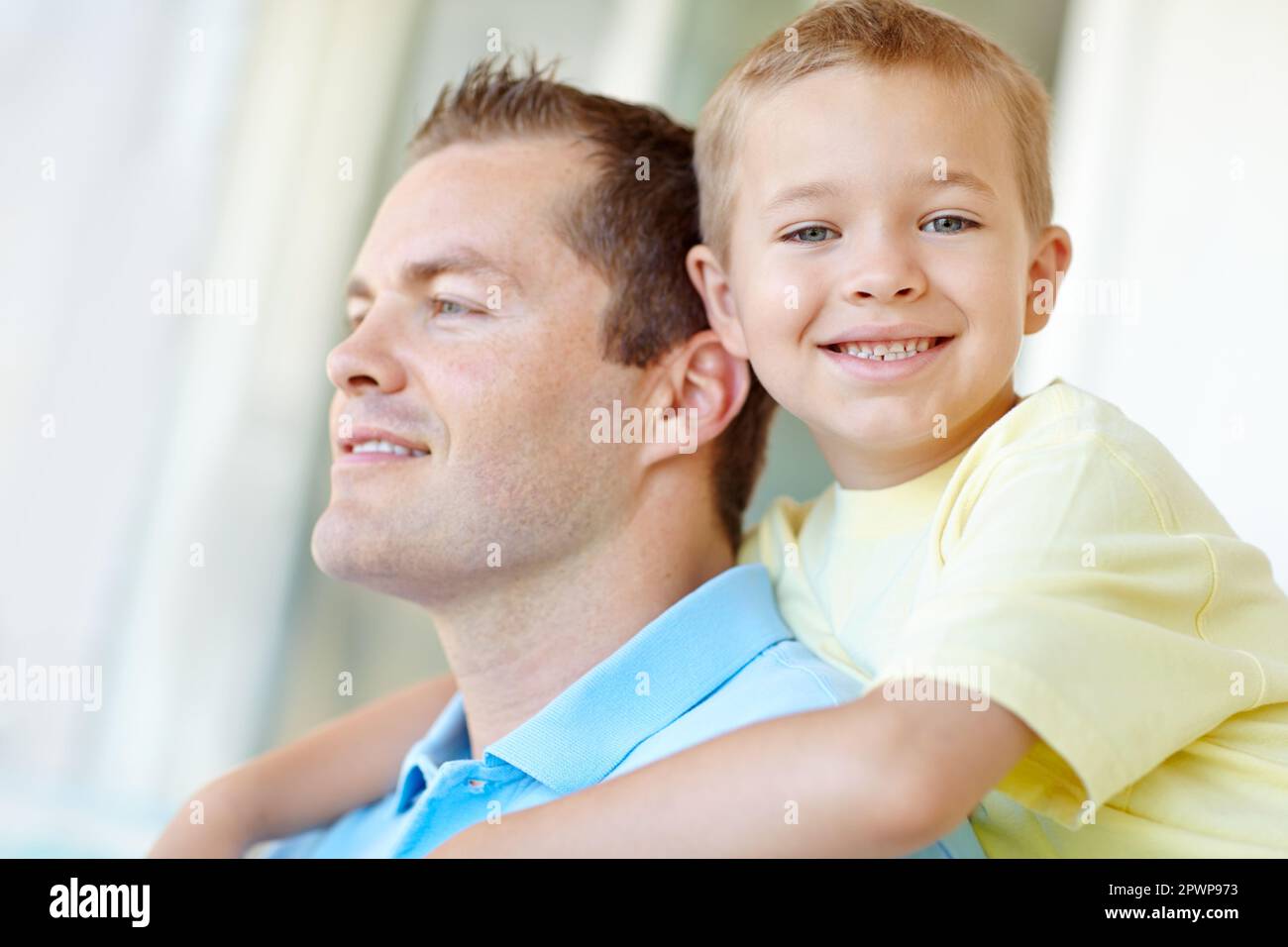 Hugging his dad. Cute, young boy smiling at the camera while hugging ...