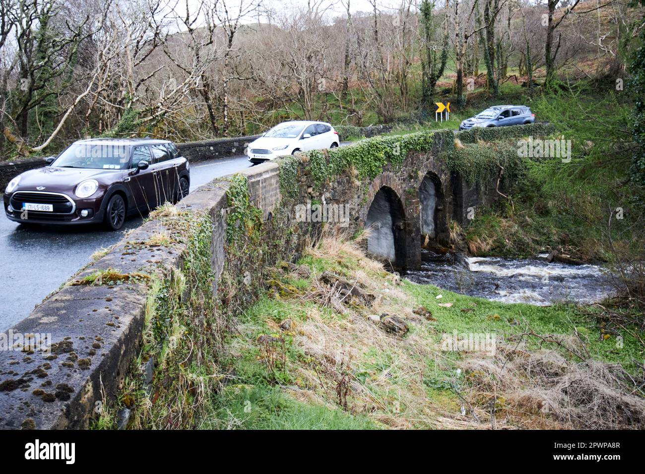 cars driving over a narrow bridge on the wild atlantic way with river ...