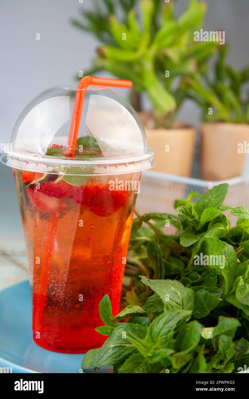 Summer mint strawberry refreshing cocktail mojito with ice in plastic glass with straw ...