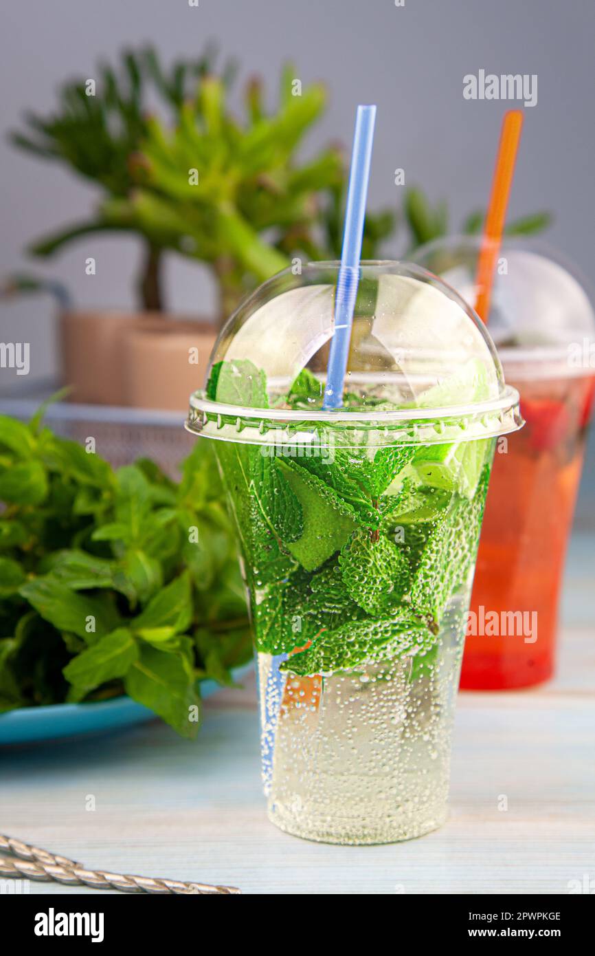 Summer mint lemon refreshing cocktail mojito with ice in plastic glass with straw. Carbonated ...