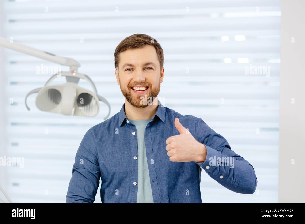 Portrait of happy patient near dental chair and shows a gesture with a ...