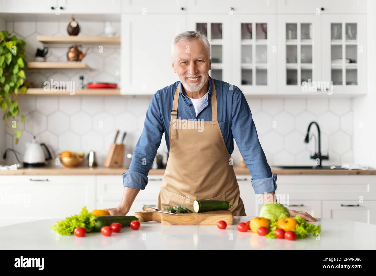 Handsome senior man posing at kitchen interior while cooking healthy ...