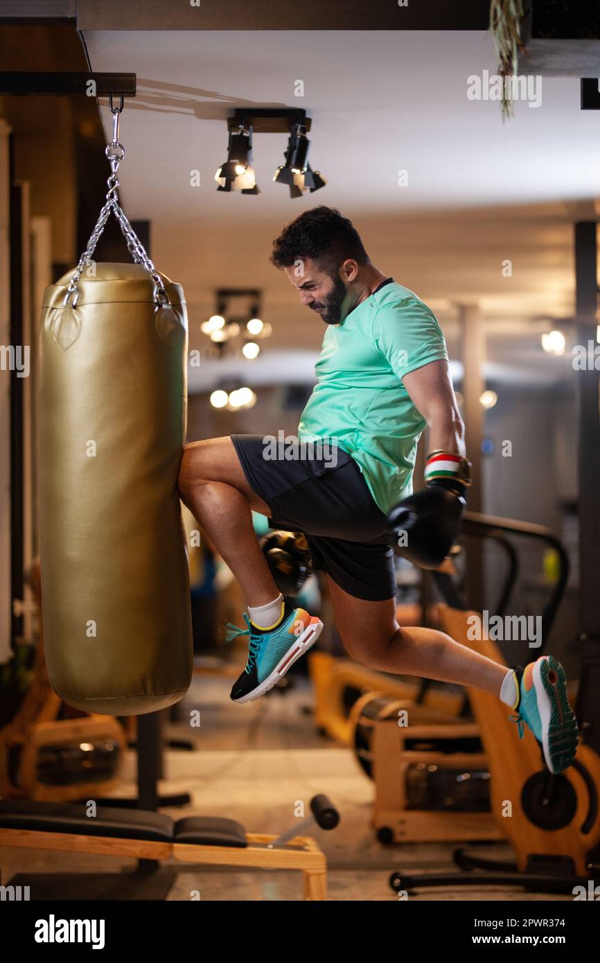 Muscular man with boxing gloves jump hitting a punching bag with a knee ...