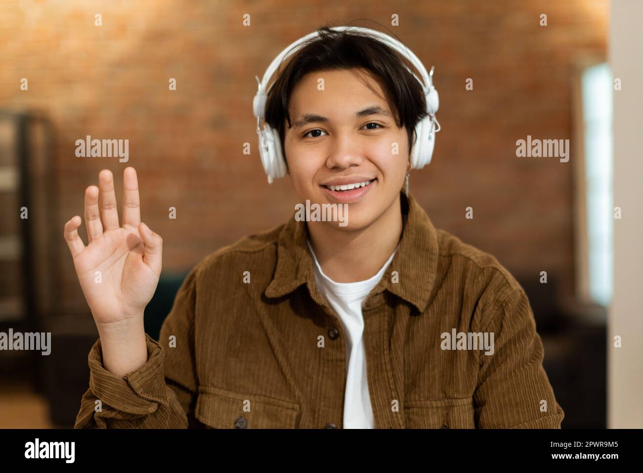 Happy Chinese Teenager Boy Wearing Earphones Waving Hello At Home Stock ...