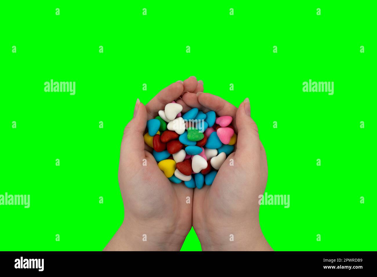 A handful of multi-colored heart-shaped candies in hands on a green ...