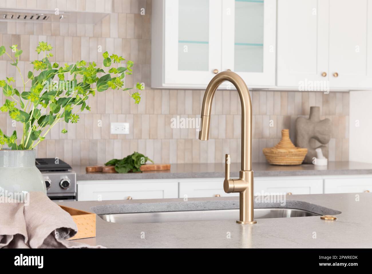 A kitchen faucet detail with a grey stone countertop island, gold ...