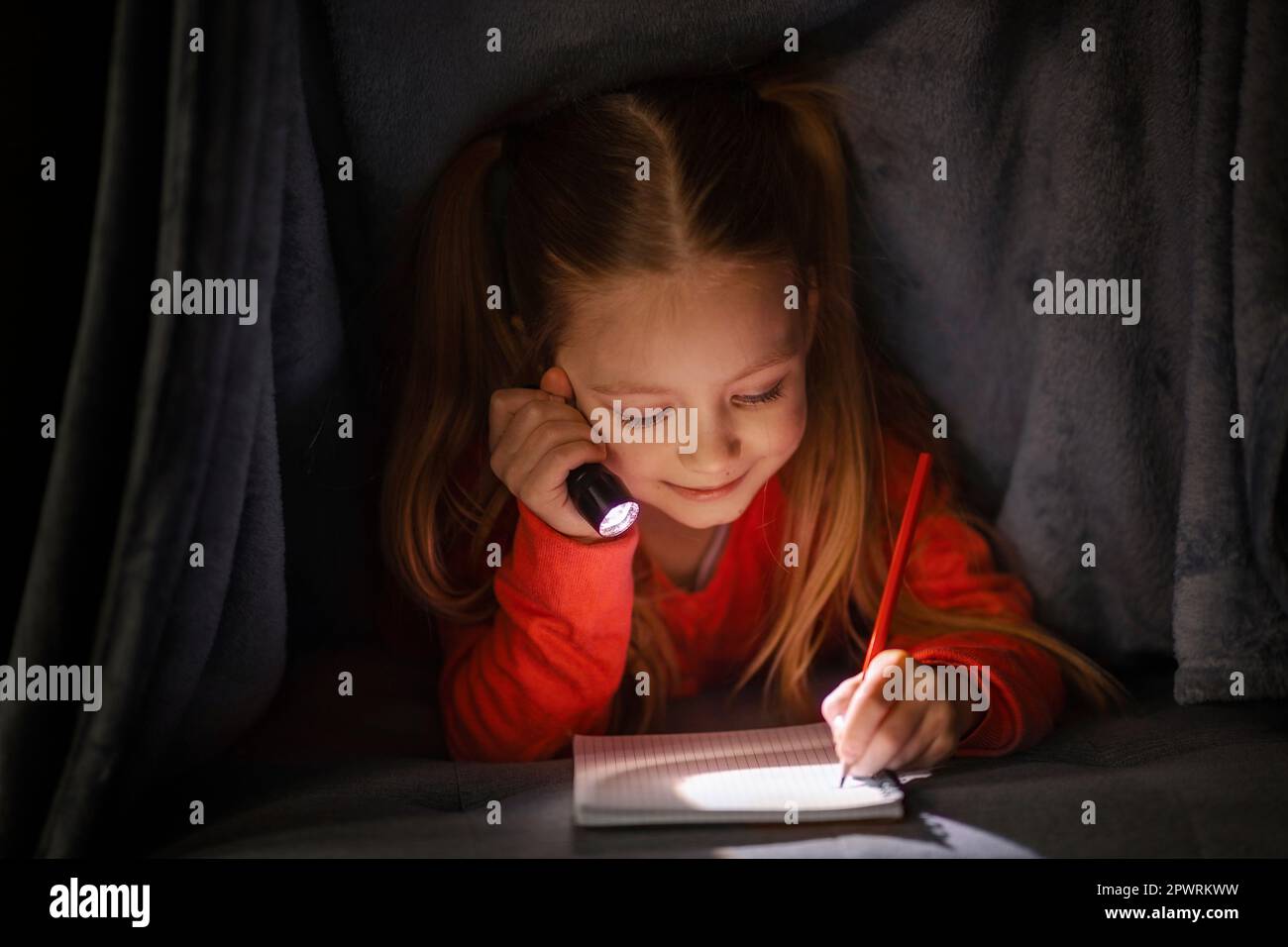 Cute Little Girl Writing In Notebook While Hiding Under Blanket With ...