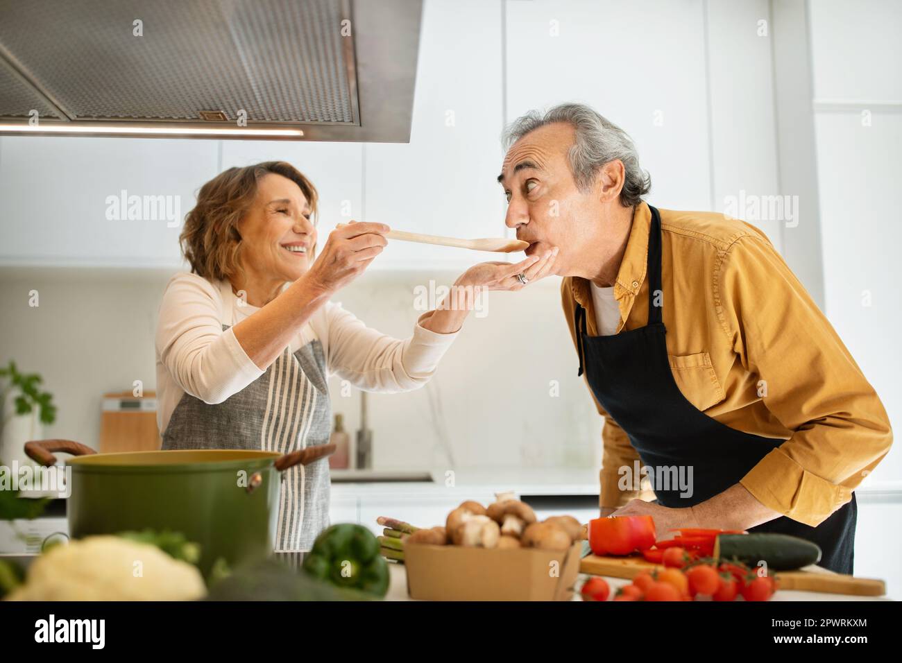 Happy senior spouses tasting food, woman giving her husband to try soup ...