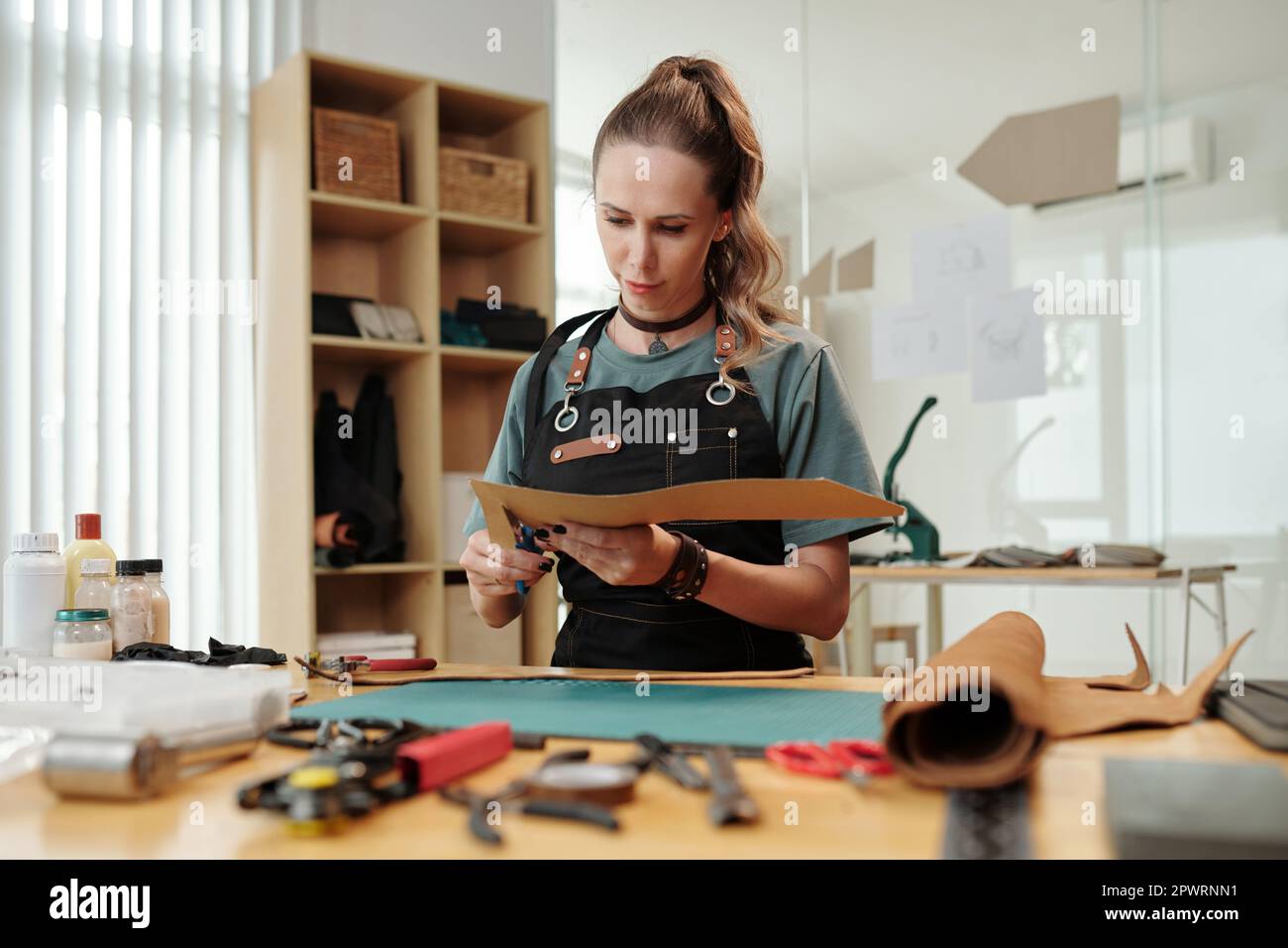 Leather crafter cutting out cardboard sewing pattern of new bag Stock ...