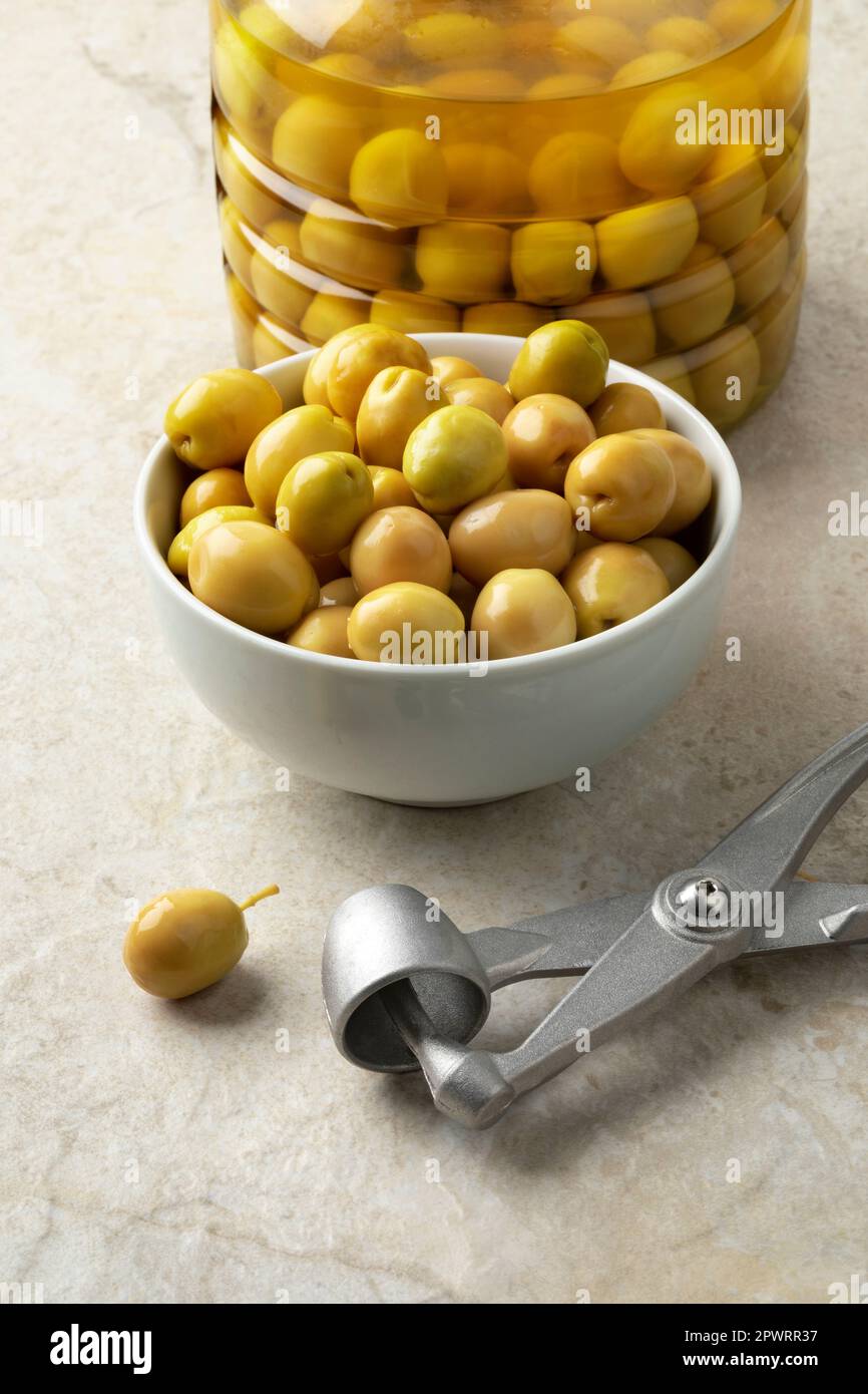 Bowl with green Turkish olives close up and a metal olive pitter and an ...