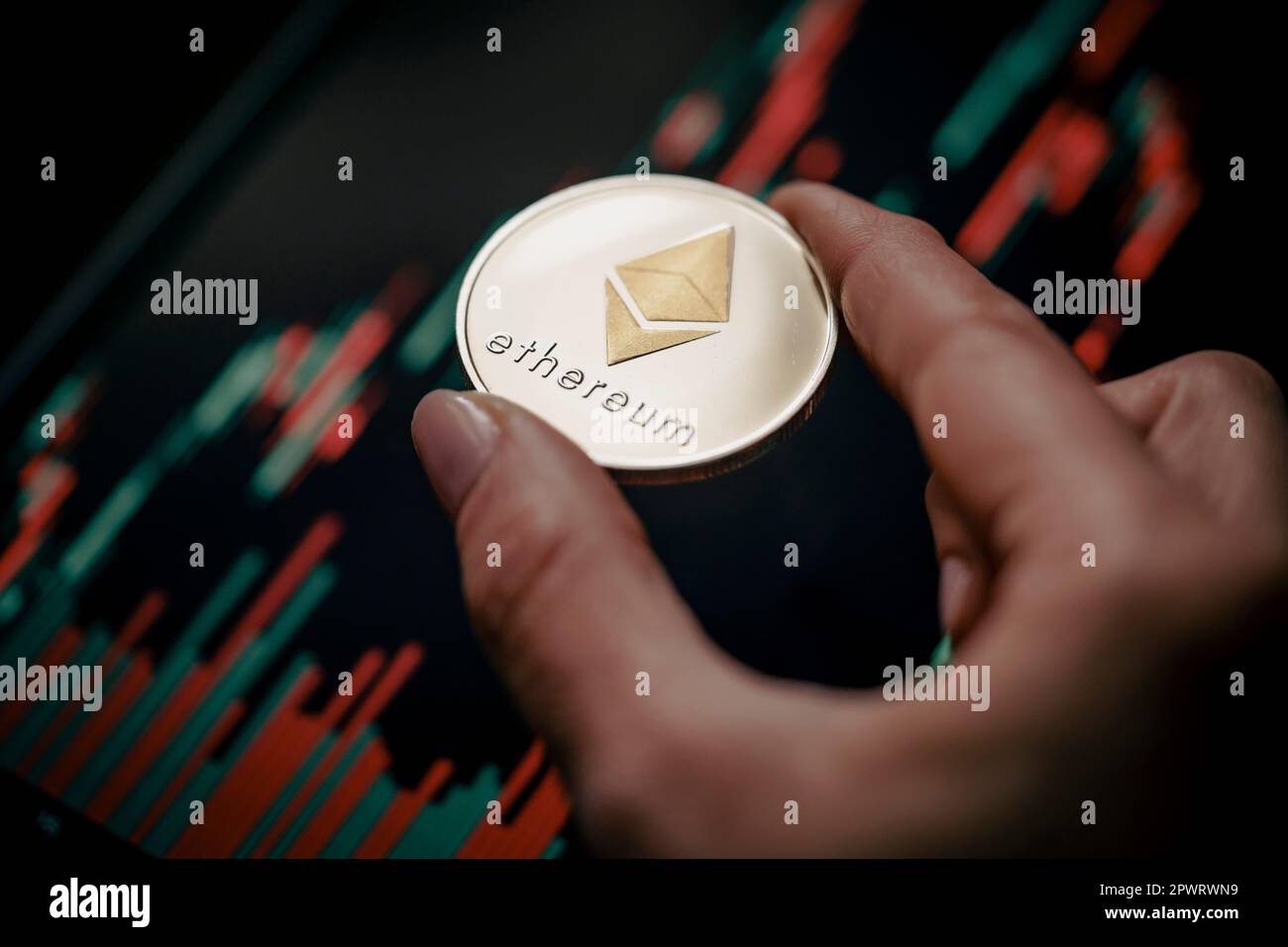 Hand holding a silver Ethereum (ETH) cryptocurrency coin with candle ...