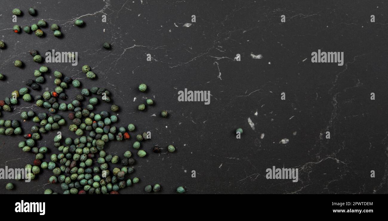 Tabletop view, Black pepper (Piper nigrum) spice spilled on dark marble ...