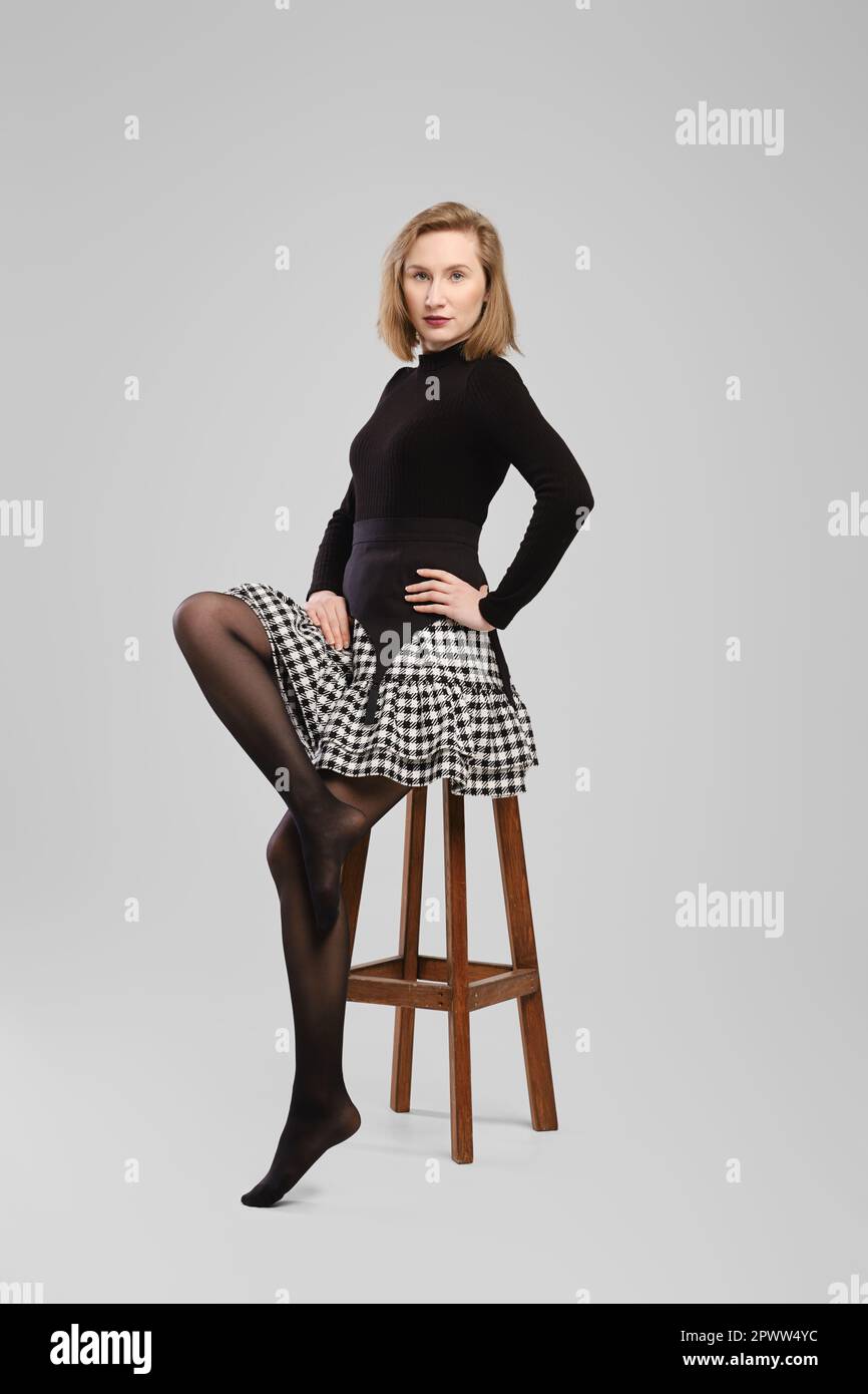 Barefoot woman in turtleneck and little skirt sitting on tall chair in ...