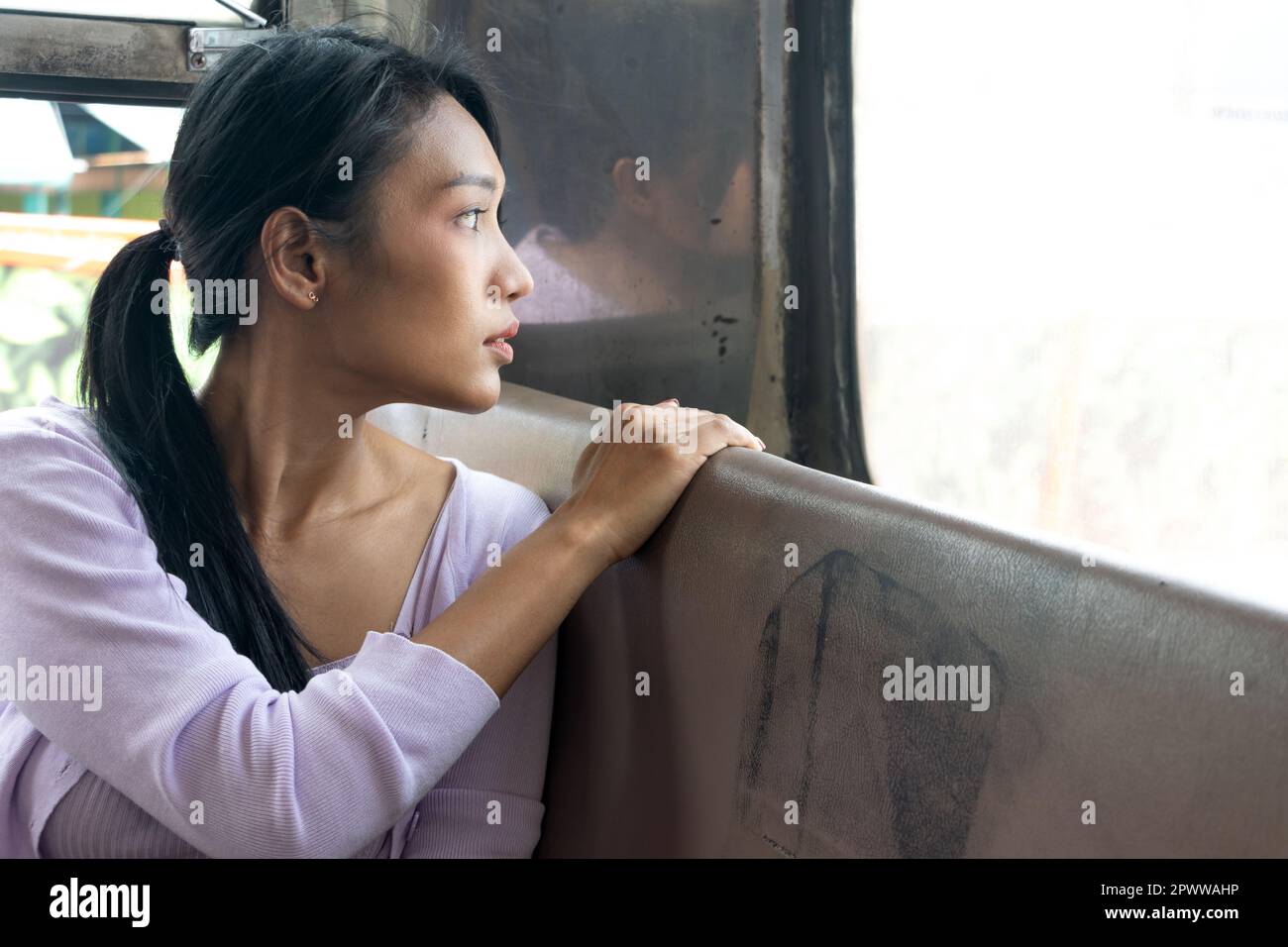 A young woman sits in a old bus and looks back through the rear window ...