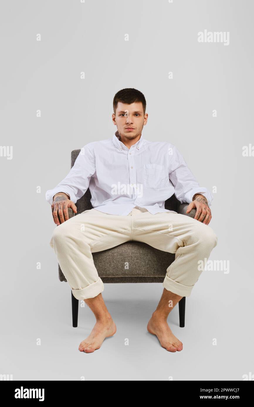 Full length studio portrait of young barefoot man in white shirt and ...