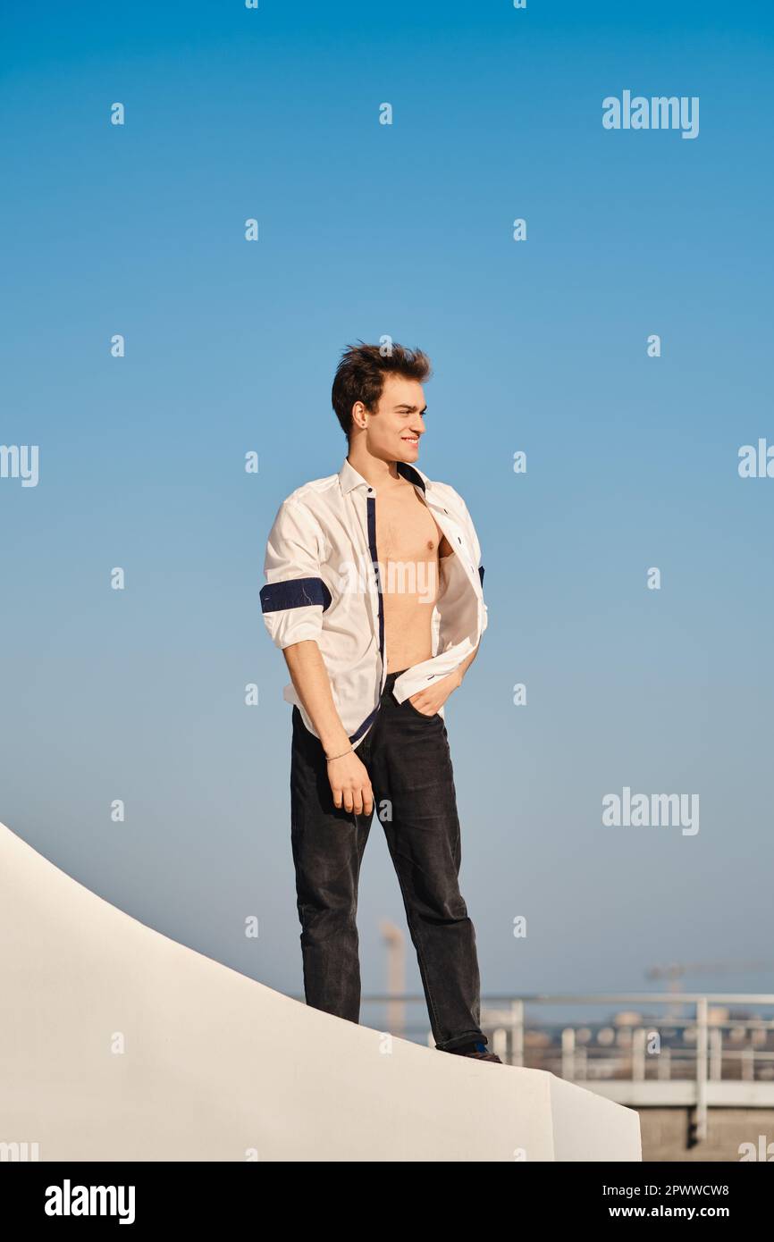 Full length portrait of a young man in unfastened white shirt on the ...
