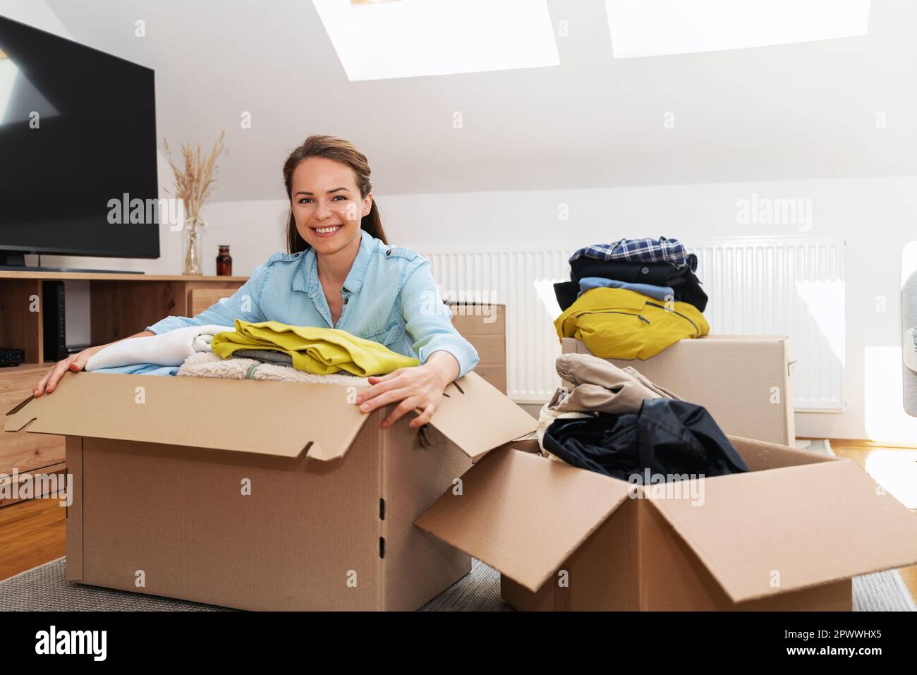 Young woman packing her own clothes to send to charitable organisation ...
