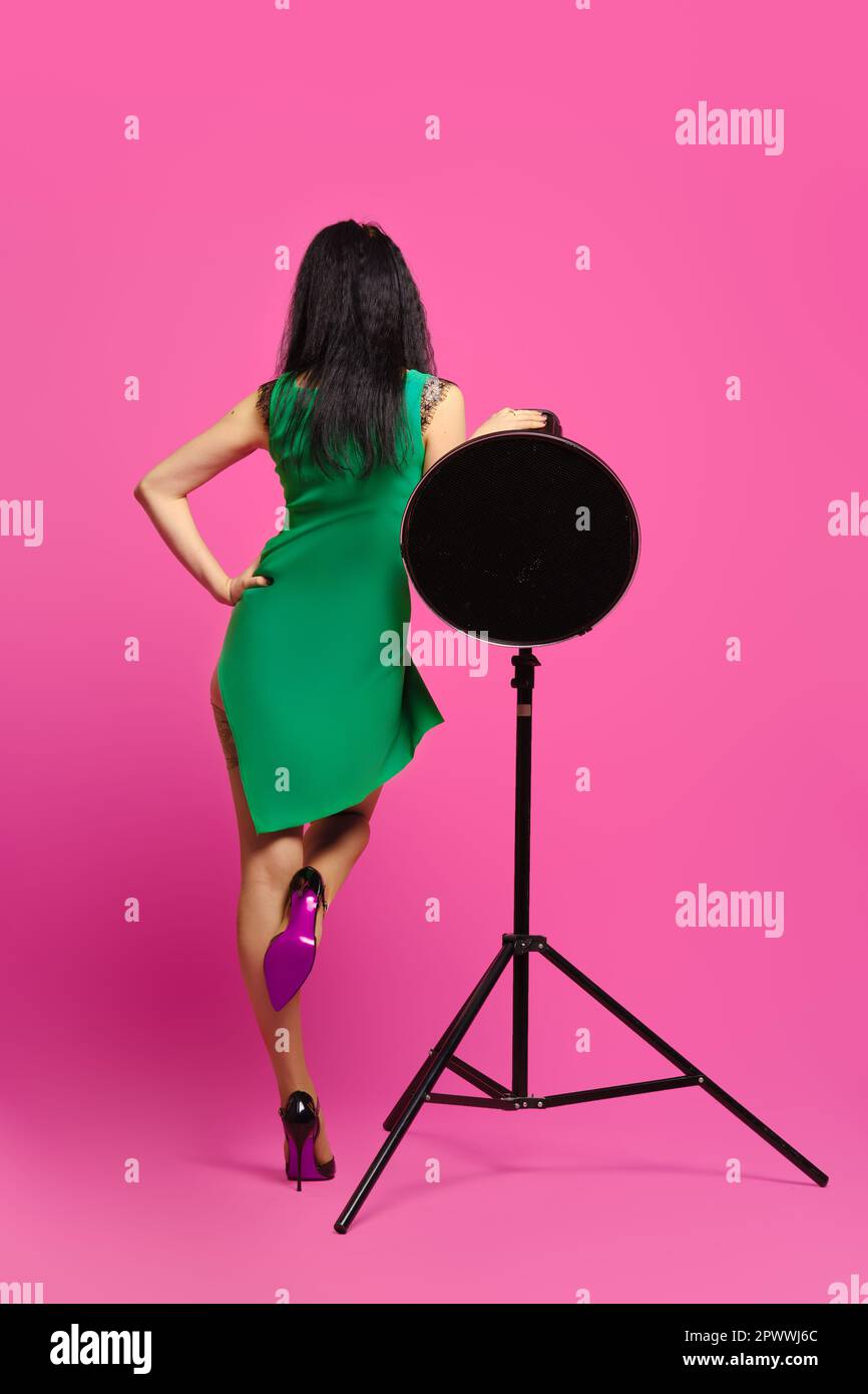Rear view of woman with black hair and in green dress rising one leg ...