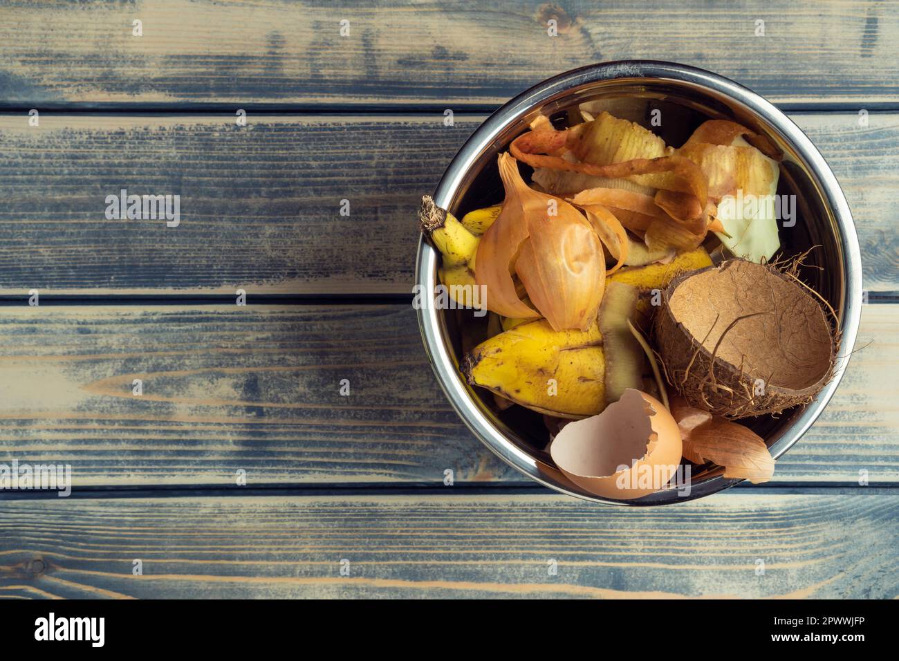 Metal bowl full organic food scraps and peel rubbish on wood background ...