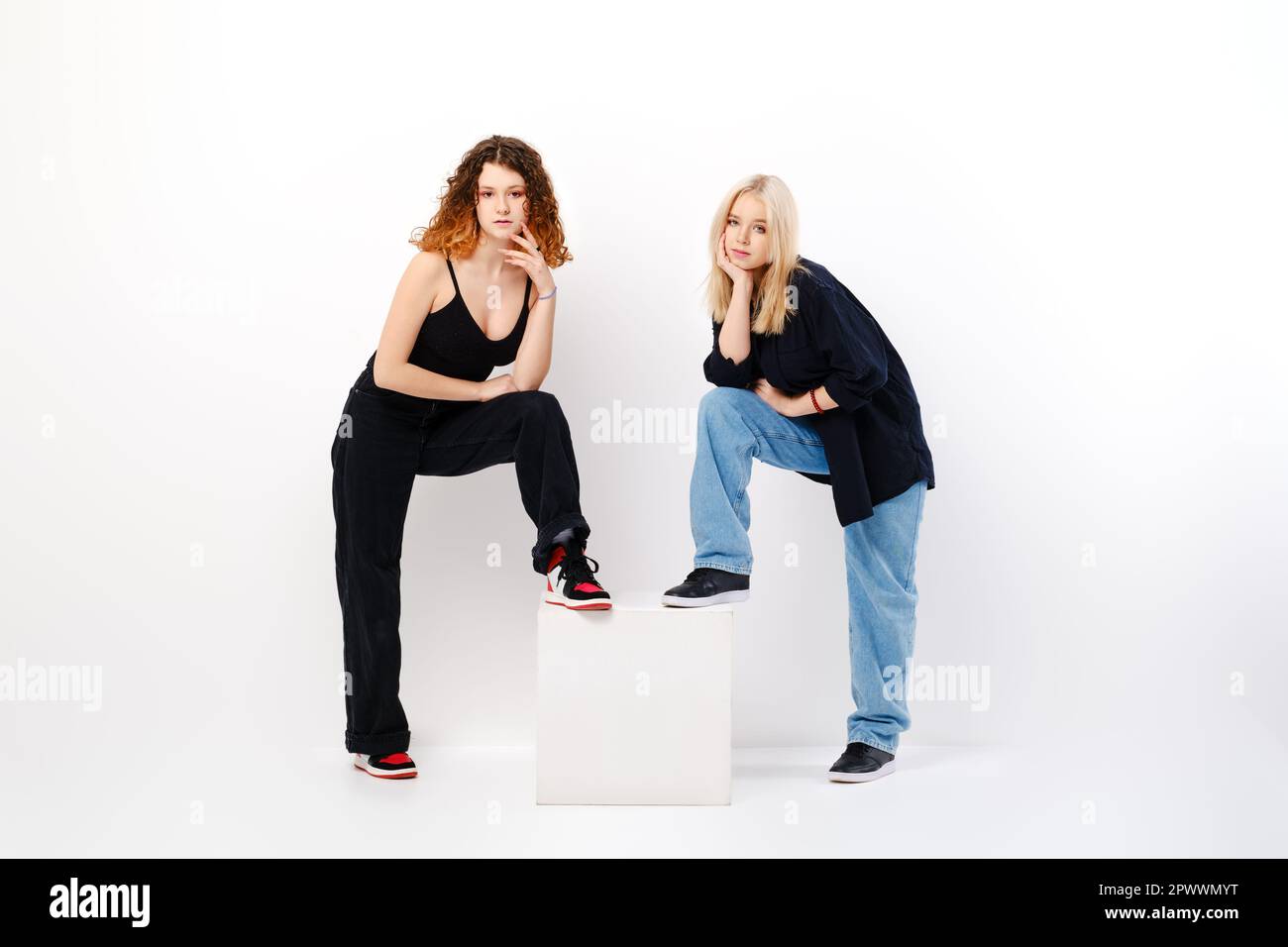 Two teen girls lean on square box over white studio background Stock ...
