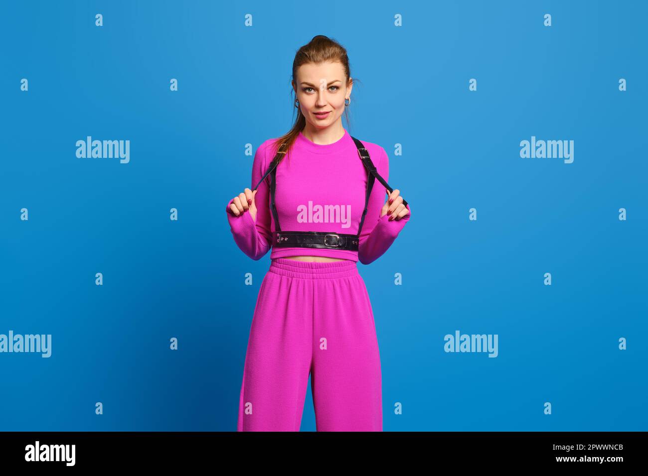 Trendy woman in purple knitted pantsuit holds the belts of leather ...
