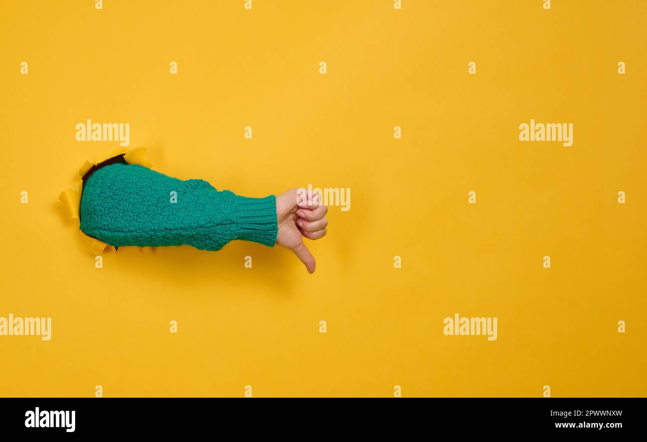 Dislike gesture break through the yellow paper. A part of the body ...