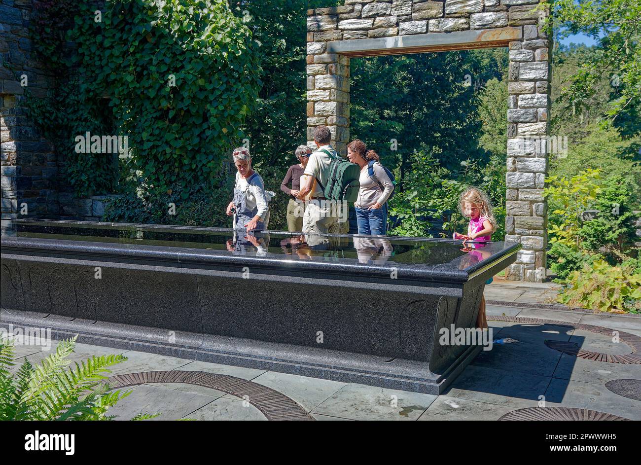 long reflective water table, people, dipping hands in water, stone arch ...