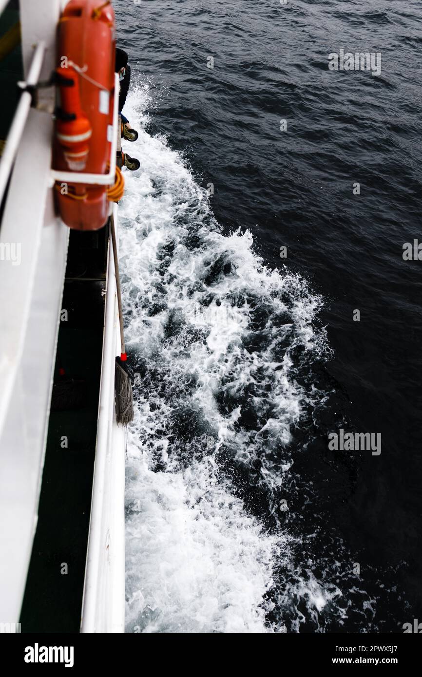 Sea splashes near a sea vessel. White yacht or ship with red lifeline ...