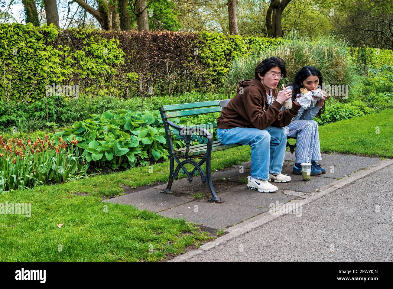 Asian Couple Eating On A City Park Bench In Spring Sunshine Concept