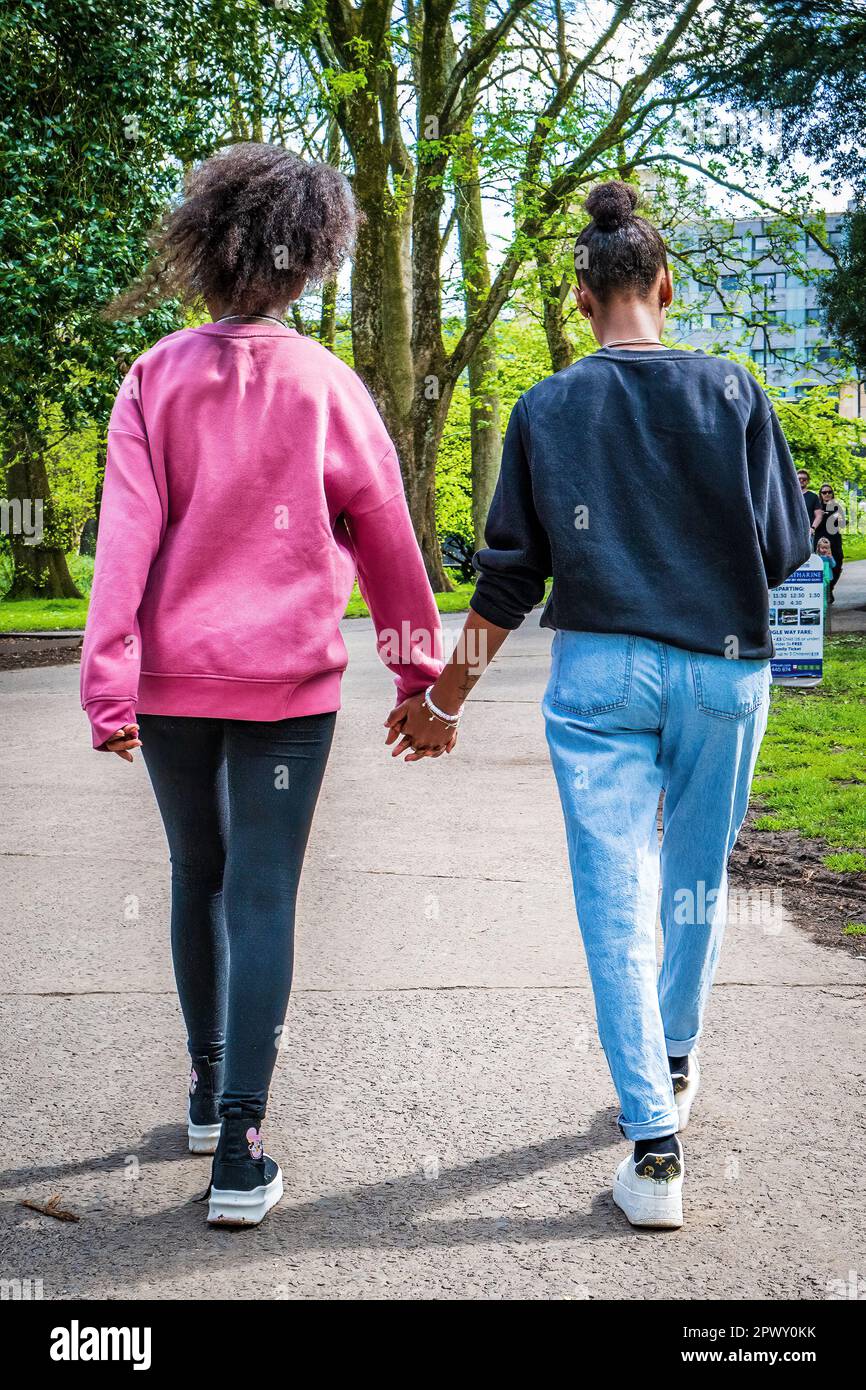Back view of two dark-skinned women holding hand and walking together ...