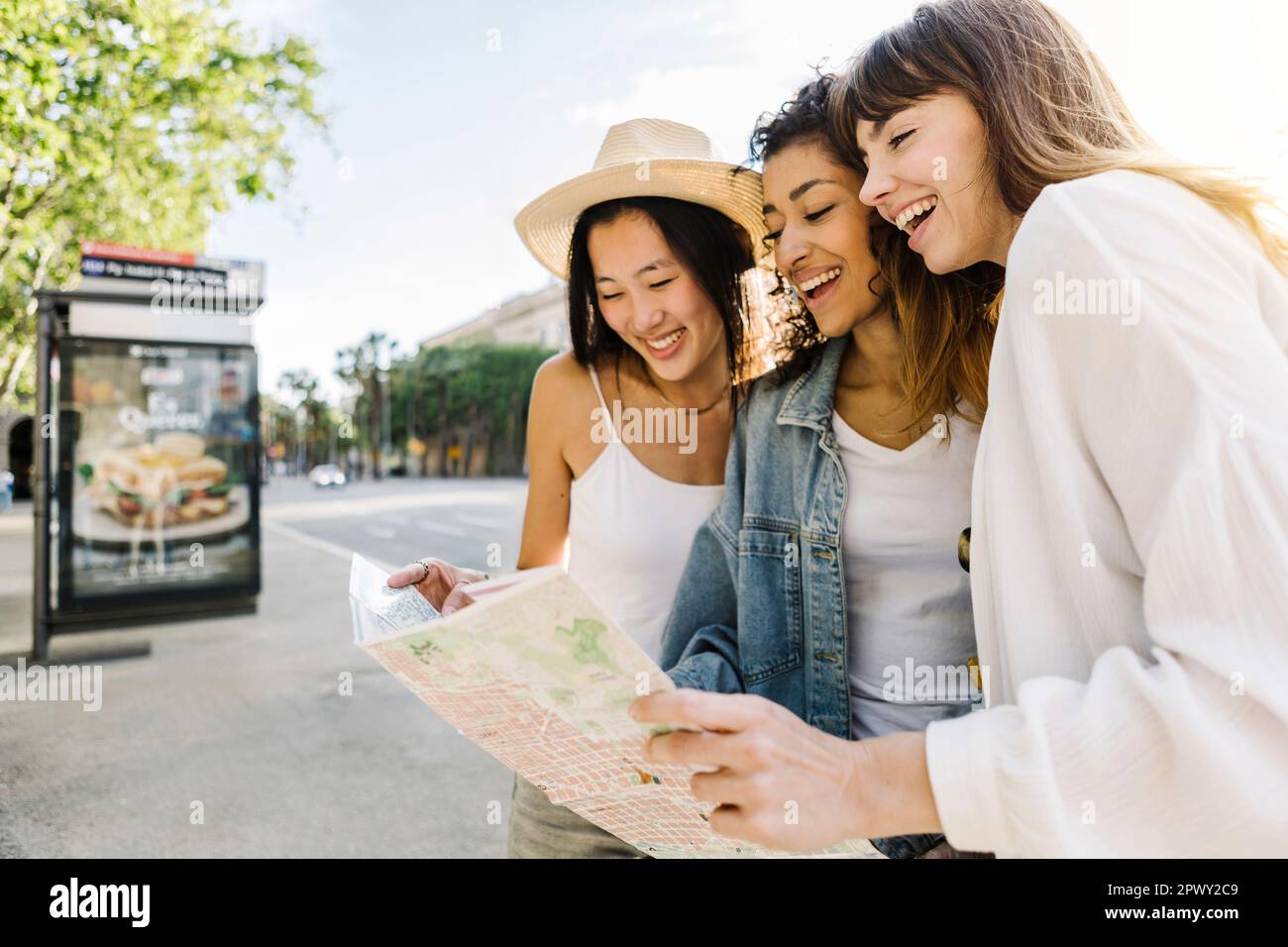 Three beautiful young adult women looking at city map while sightseeing ...