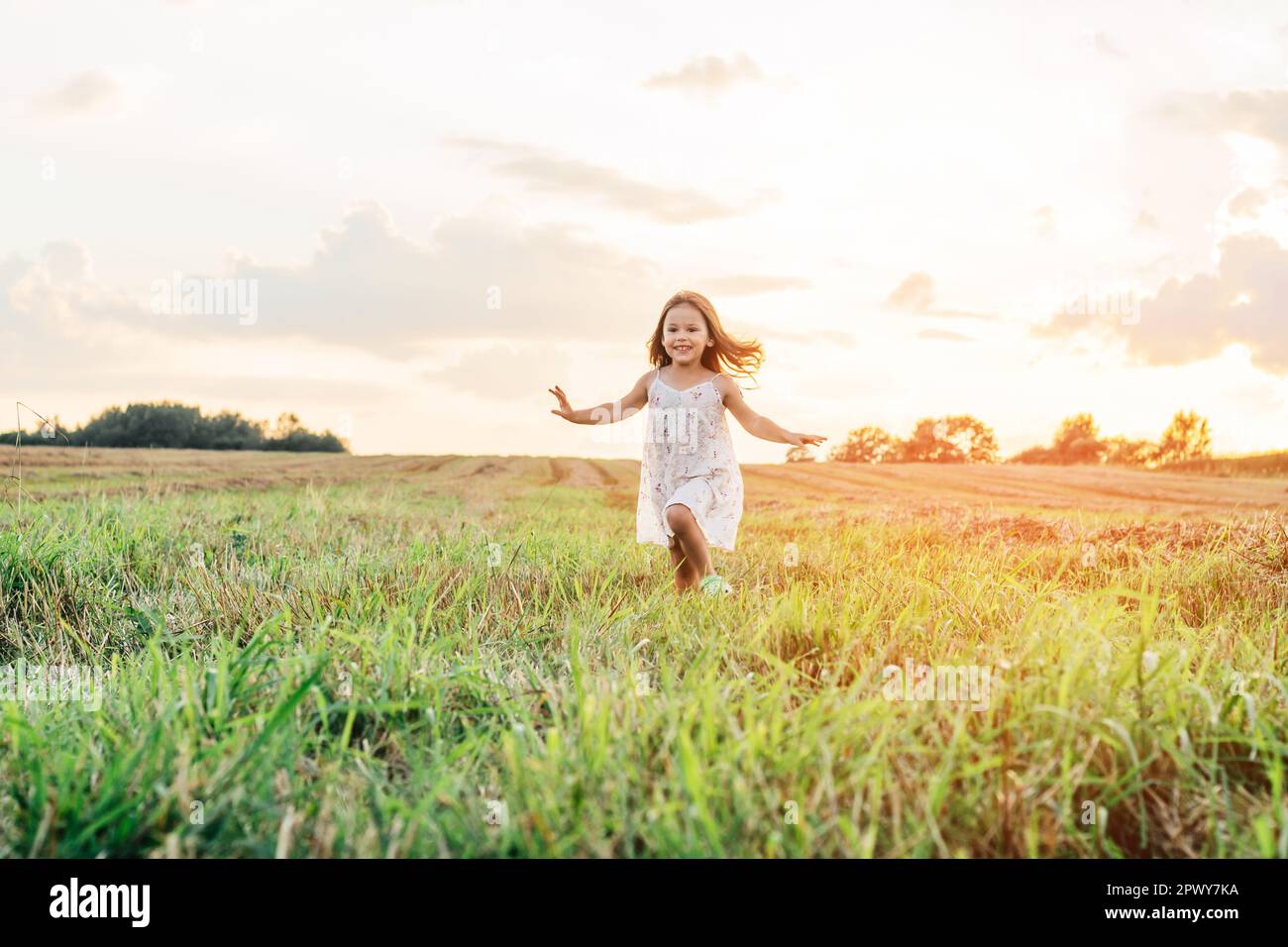 Portrait of smiling girl playing, jumping and running on grass hay ...