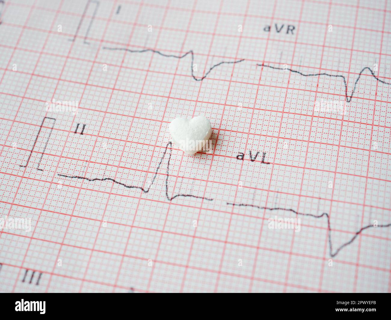 White heart-shaped tablet on paper ECG results as background. Medical ...