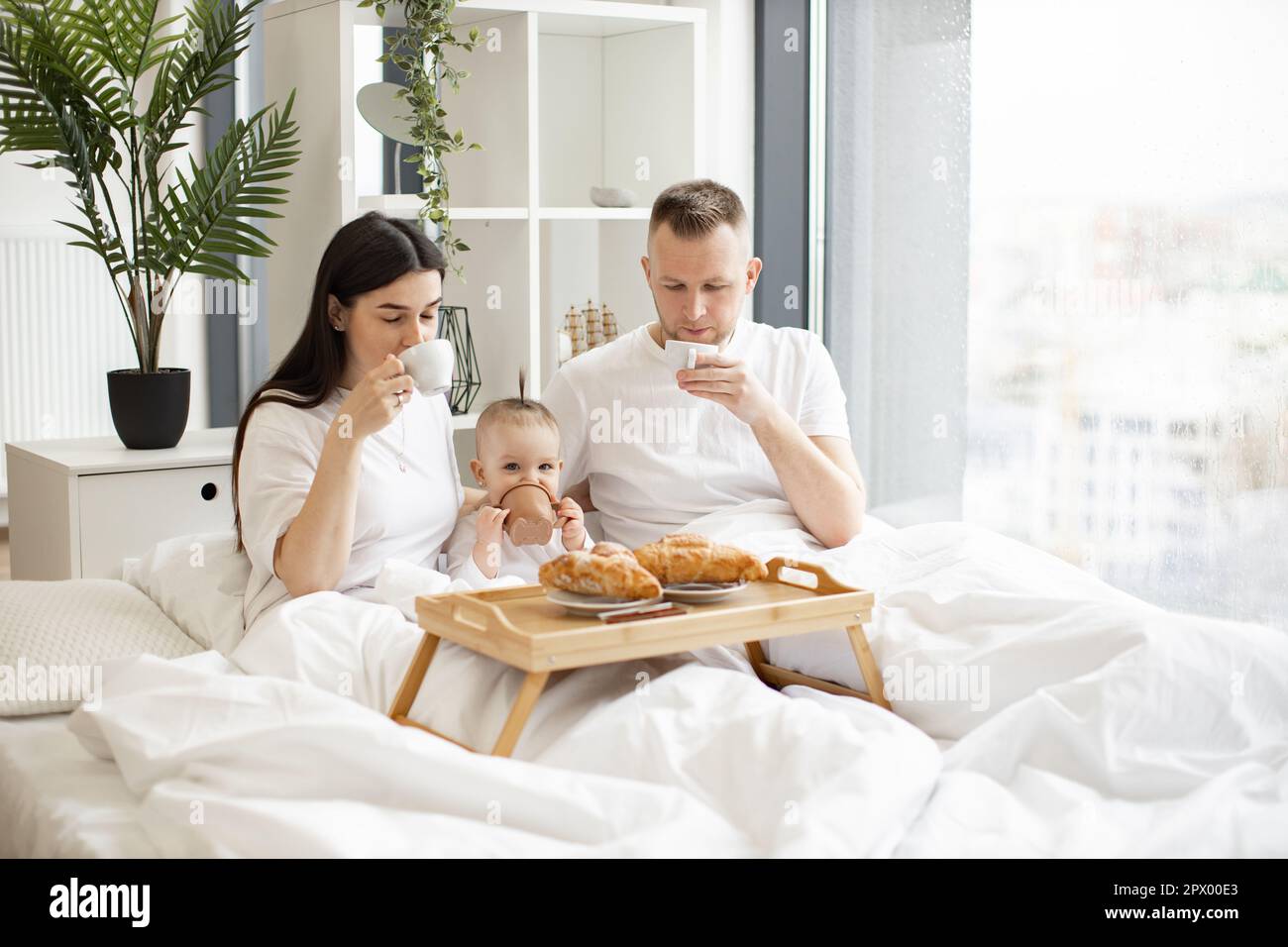 Young spouses and cute baby girl sitting under soft duvet while having ...