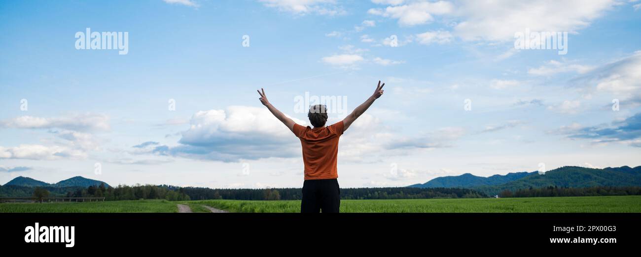 View from behind of a young man with his arms raised in victorious ...