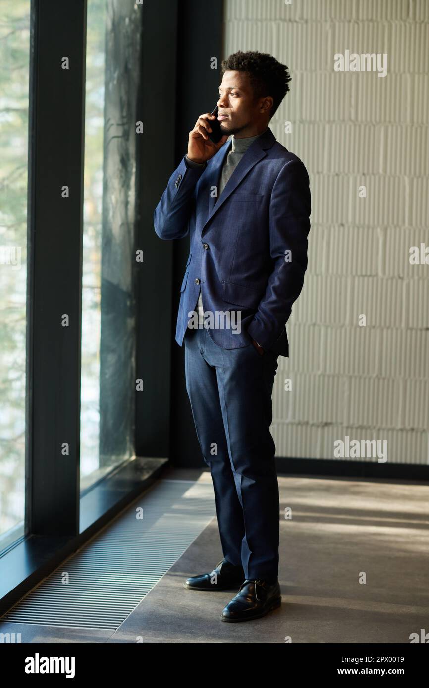 Young confident African American agent in suit talking on smartphone to ...