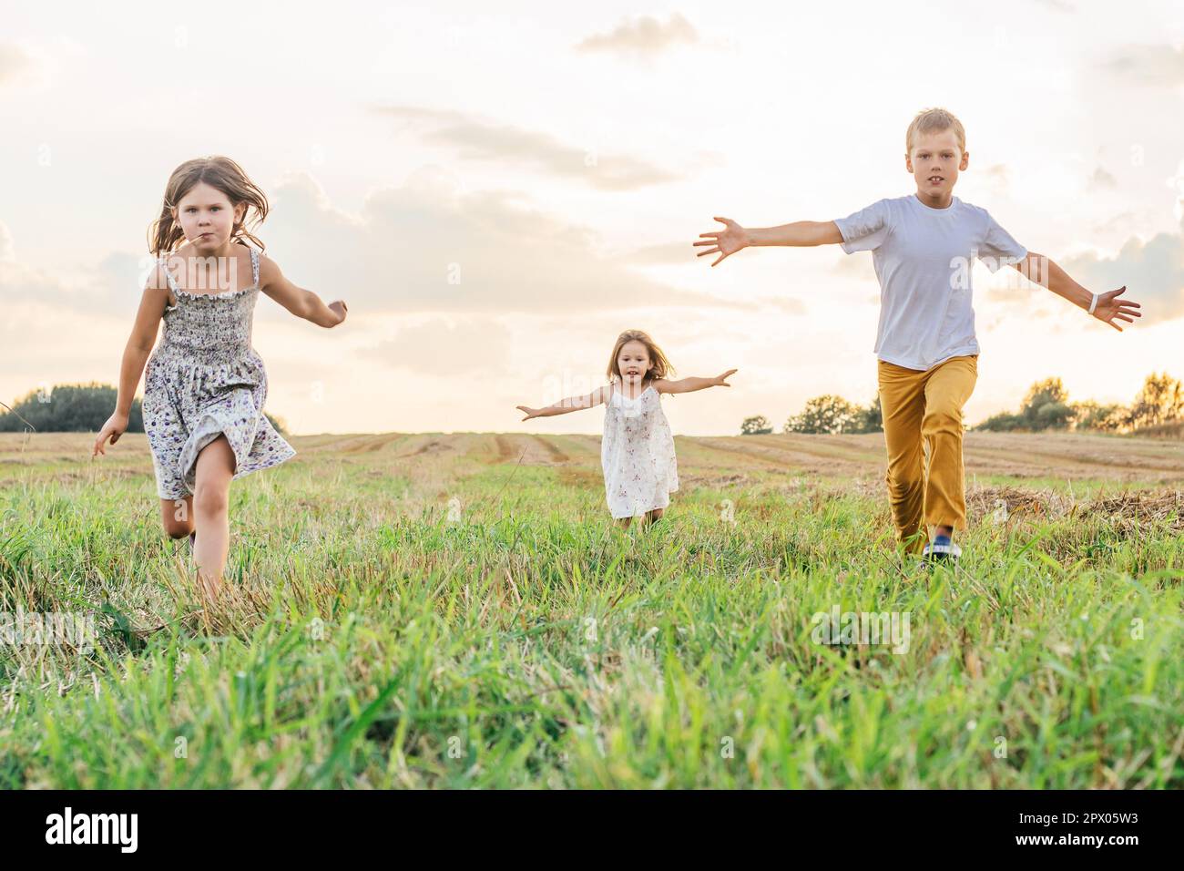 Happy little children joyfully run forward across field waving arms ...