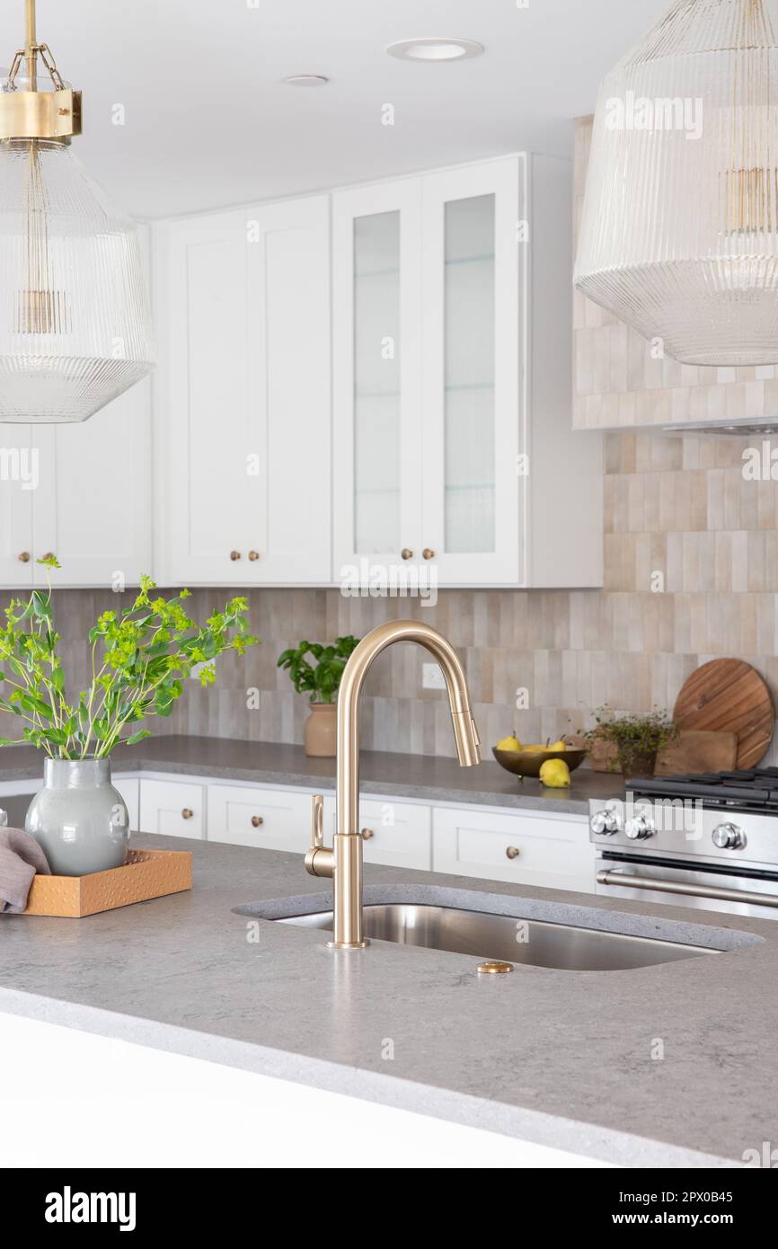 A kitchen faucet detail with a grey stone countertop island, gold ...