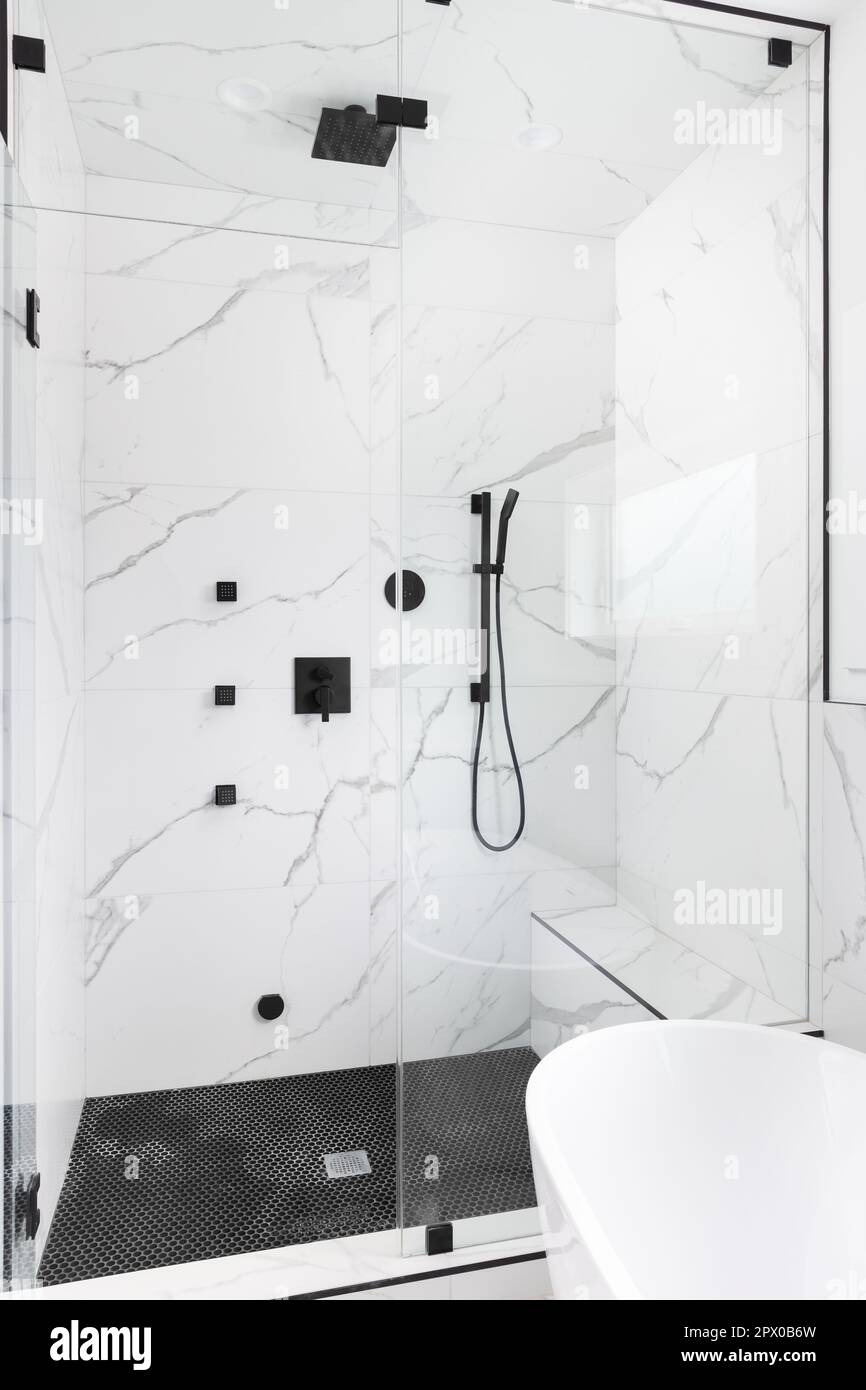 A beautiful walk-in shower with marble tiled walls, black circular tile ...
