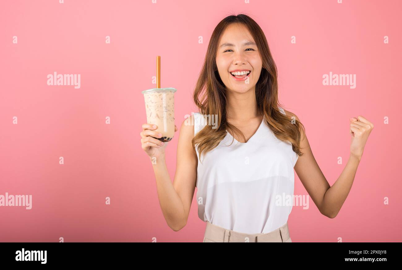 Excited Asian beautiful woman holding drinking brown sugar flavored tapioca pearl bubble milk ...
