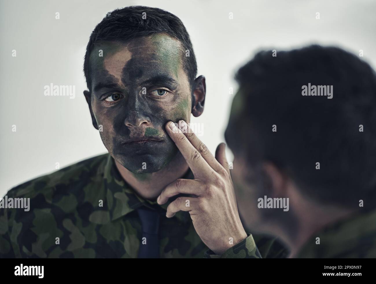 Ready for war. A young military examining his camouflaged face in the ...