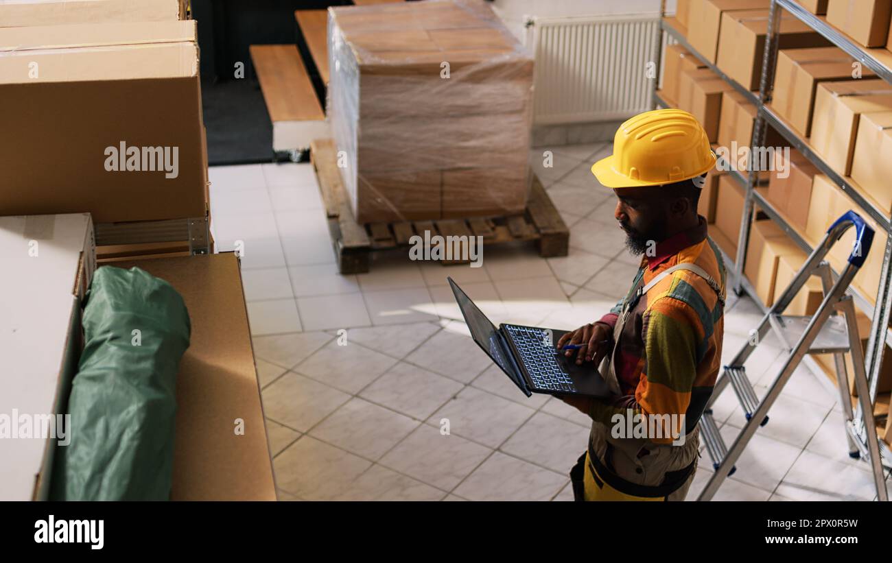 Small business worker examining cargo with laptop, reviewing quality ...