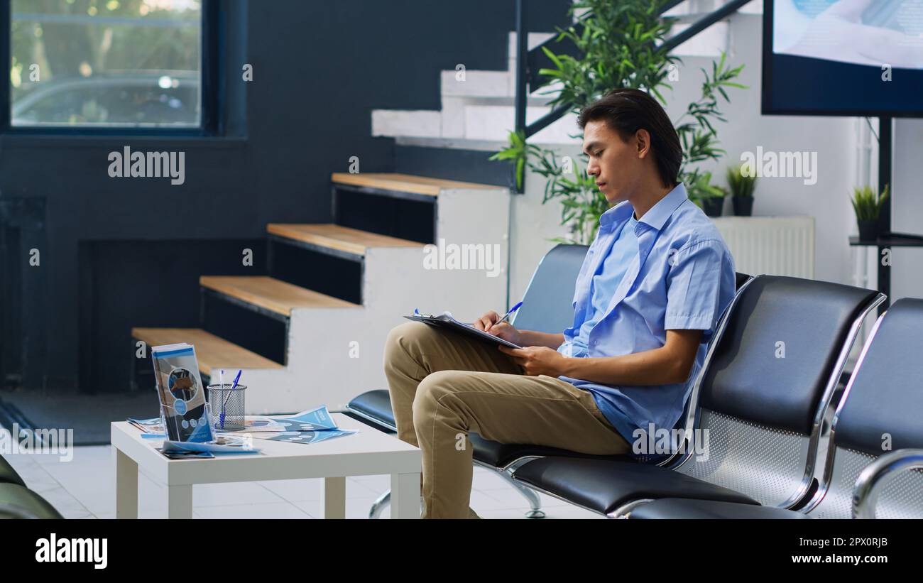 Asian patient sitting on chiar in hospital waiting area, filling ...