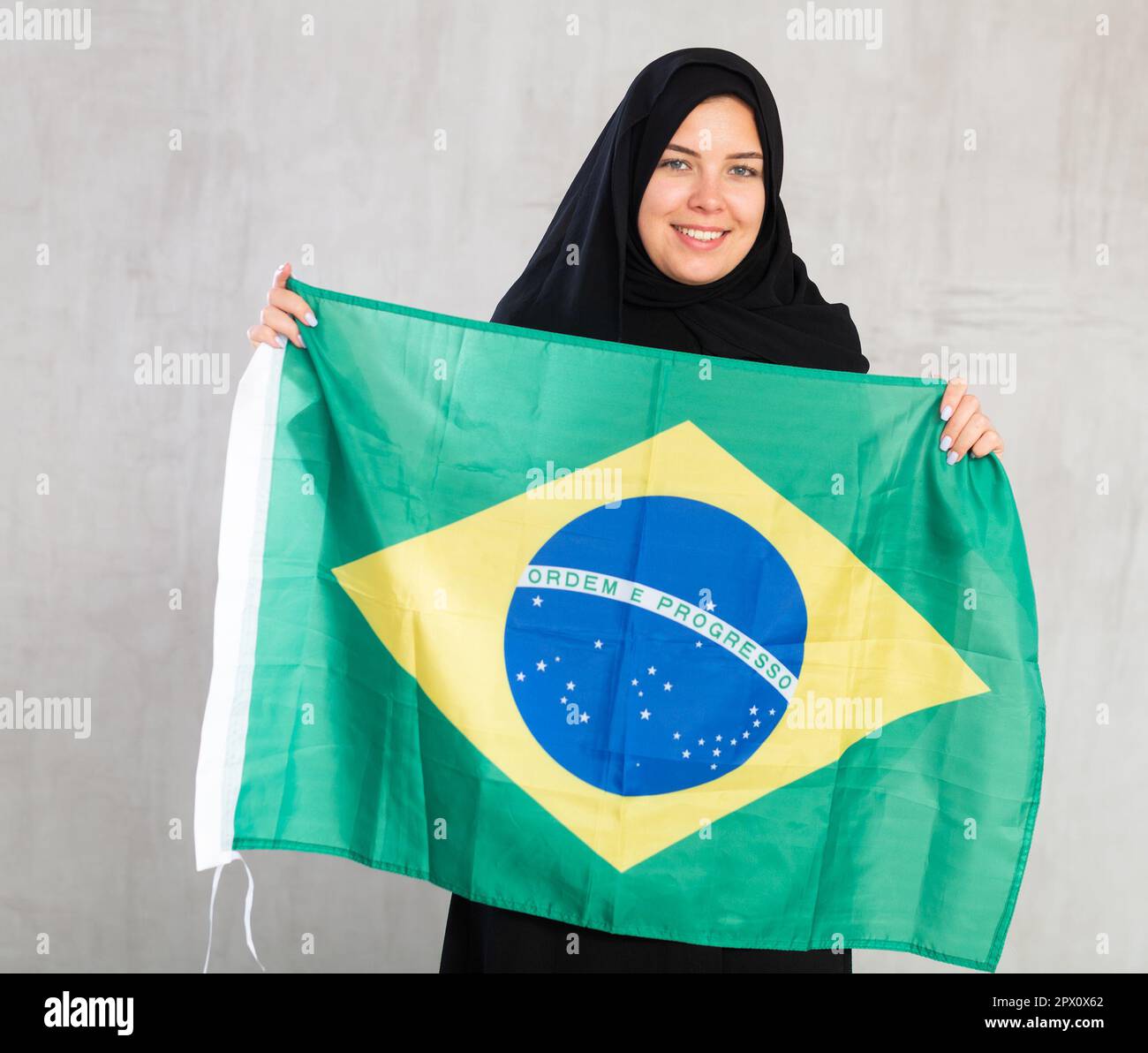 Balanced smiling Muslim woman in traditional black hijab holds flag of ...